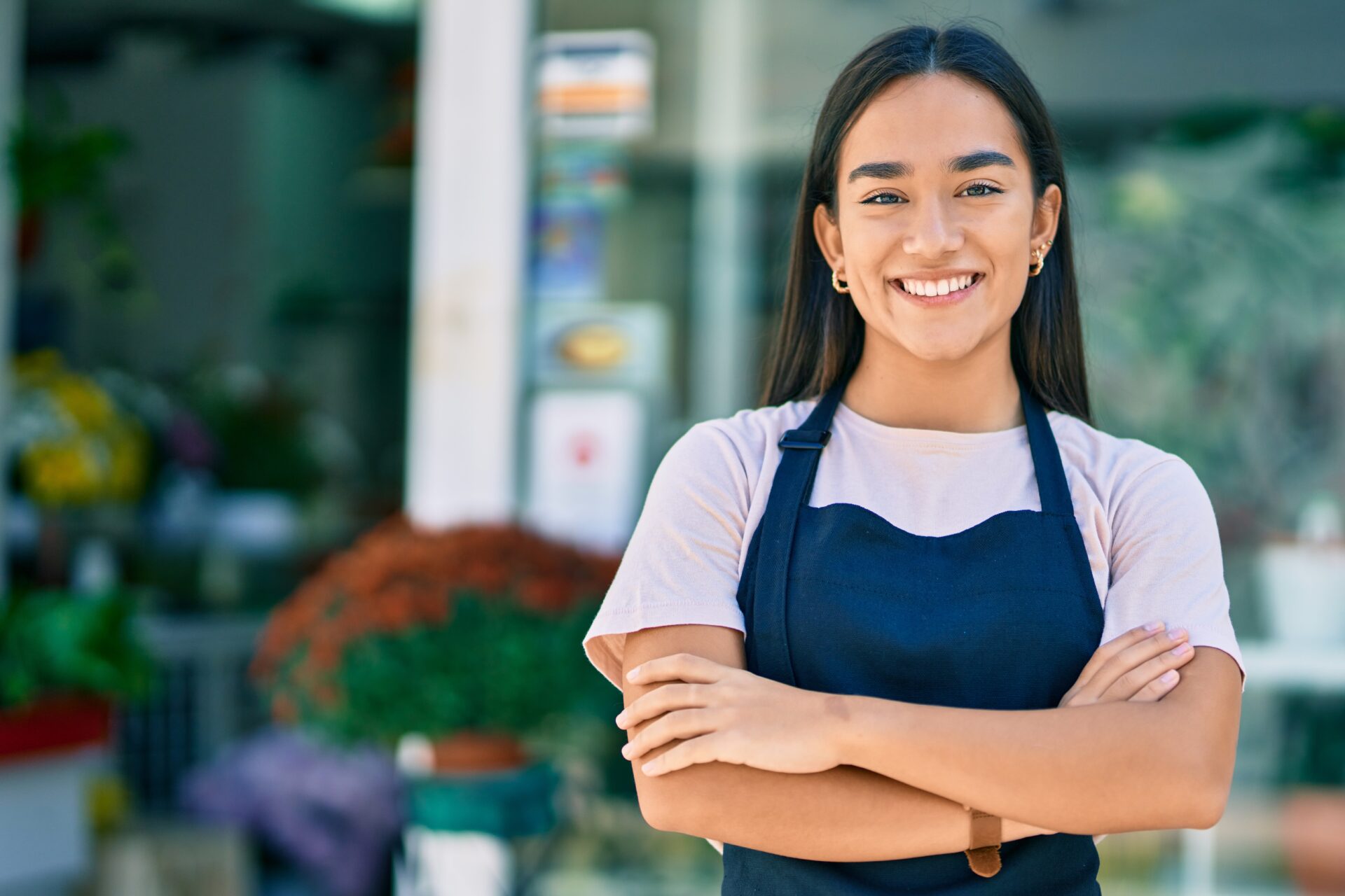 Young latin shopkeeper girl with arms crossed smiling happy standing at ...